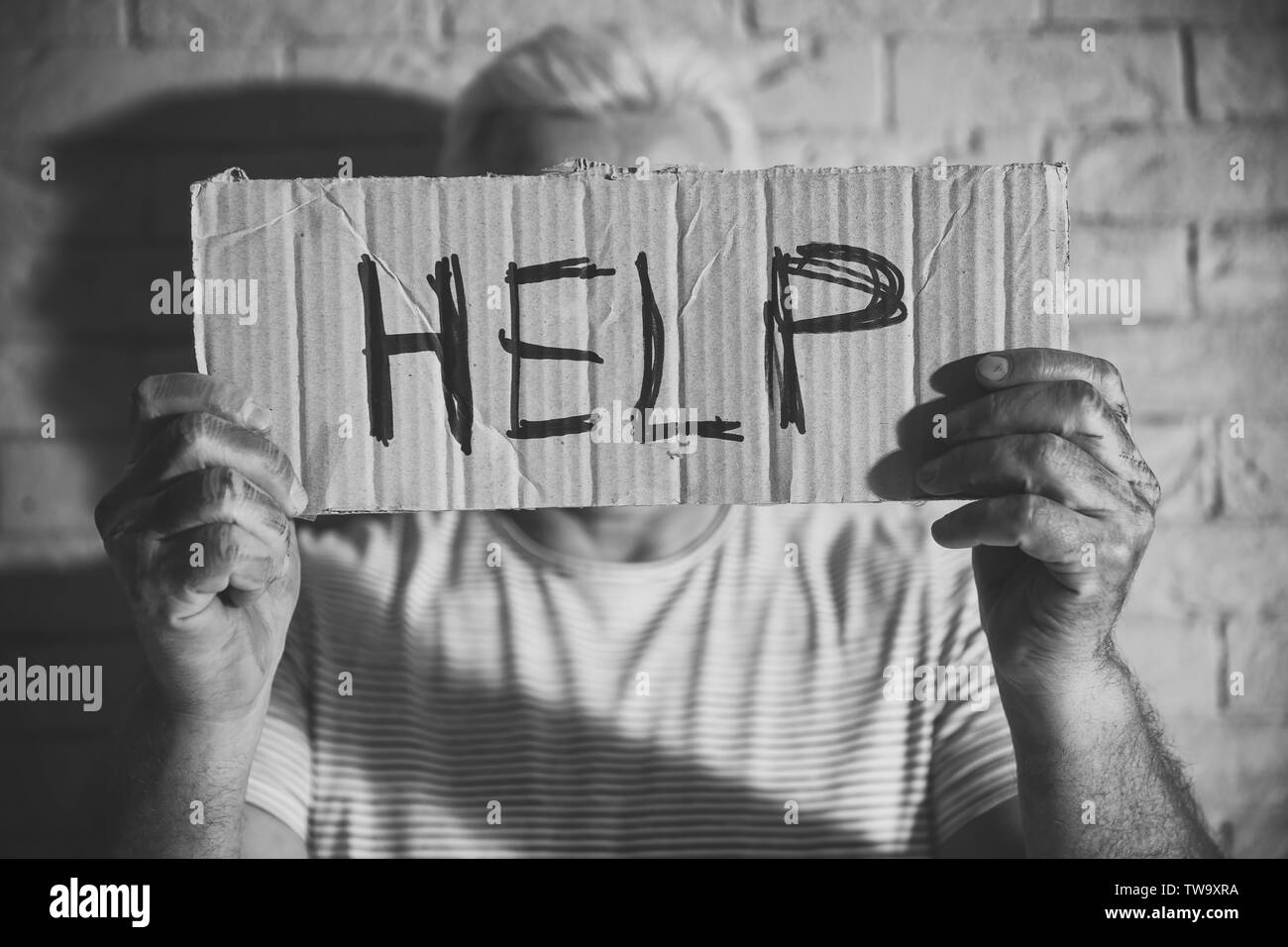 Poor man holding sign with word HELP on brick wall background. Black ...