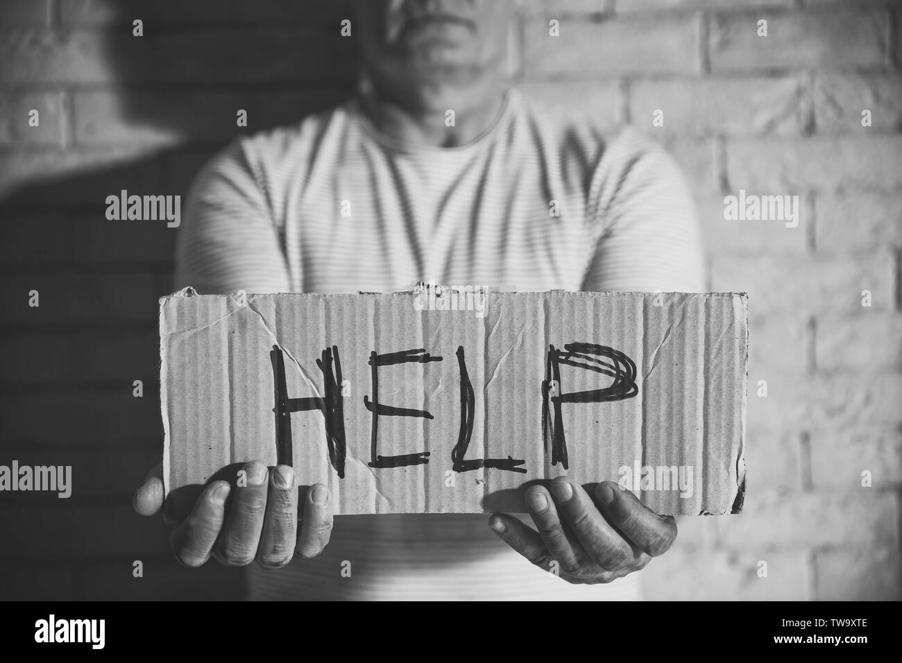 Poor man holding sign with word HELP on brick wall background. Black ...