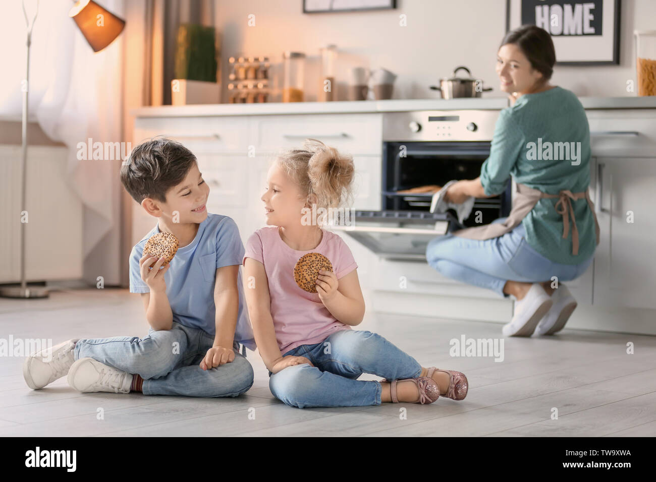 Little kids eating cookies near oven in kitchen while their mother ...
