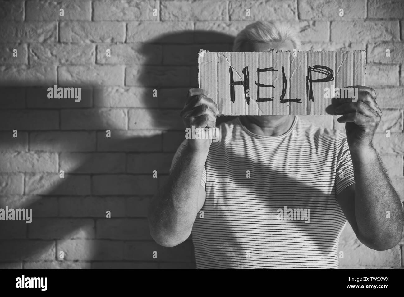 Poor man holding sign with word HELP on brick wall background. Black ...