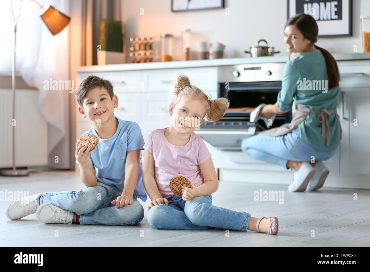 Little kids eating cookies near oven in kitchen while their mother ...