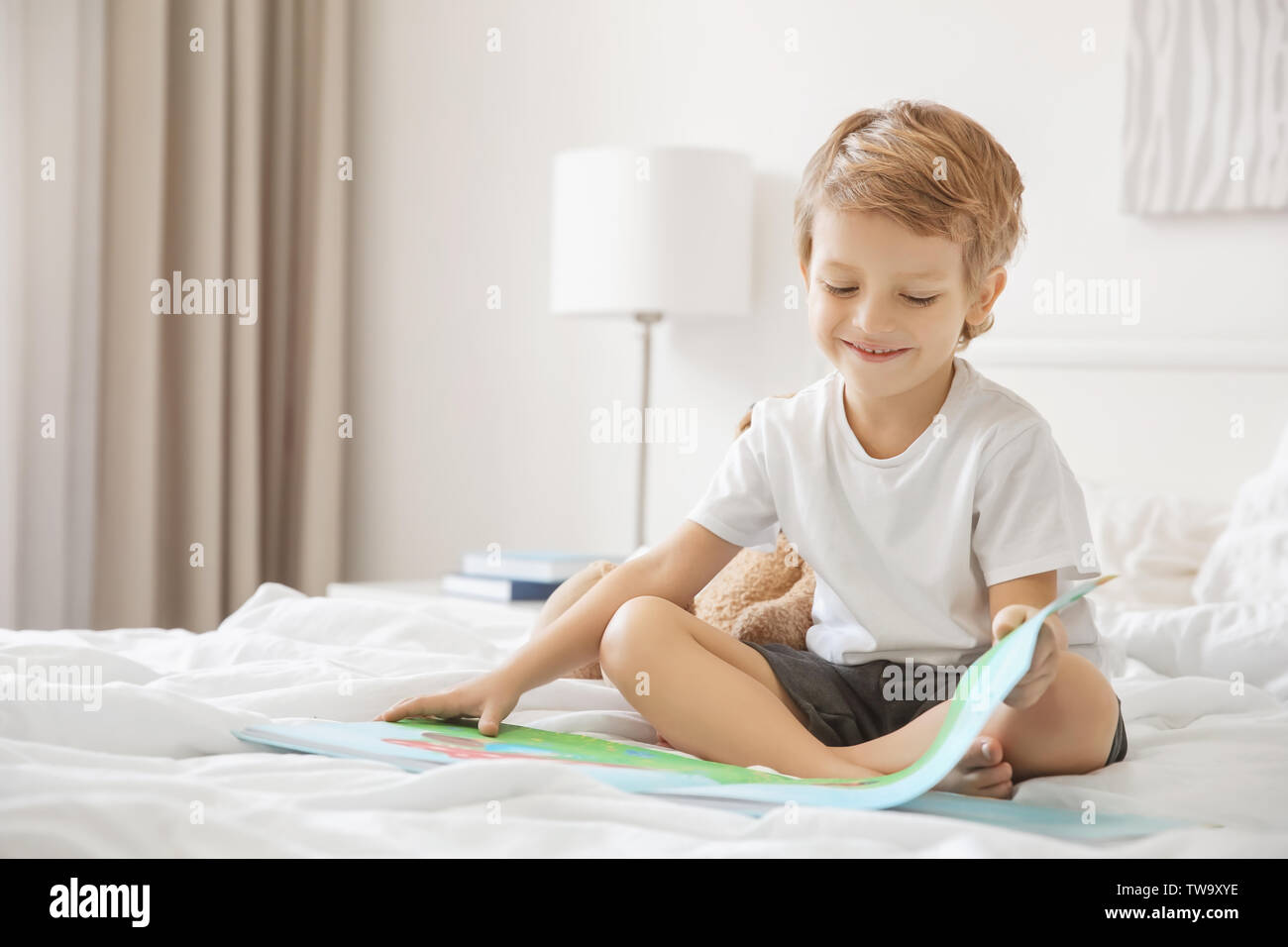 Cute boy reading book on bed at home Stock Photo - Alamy