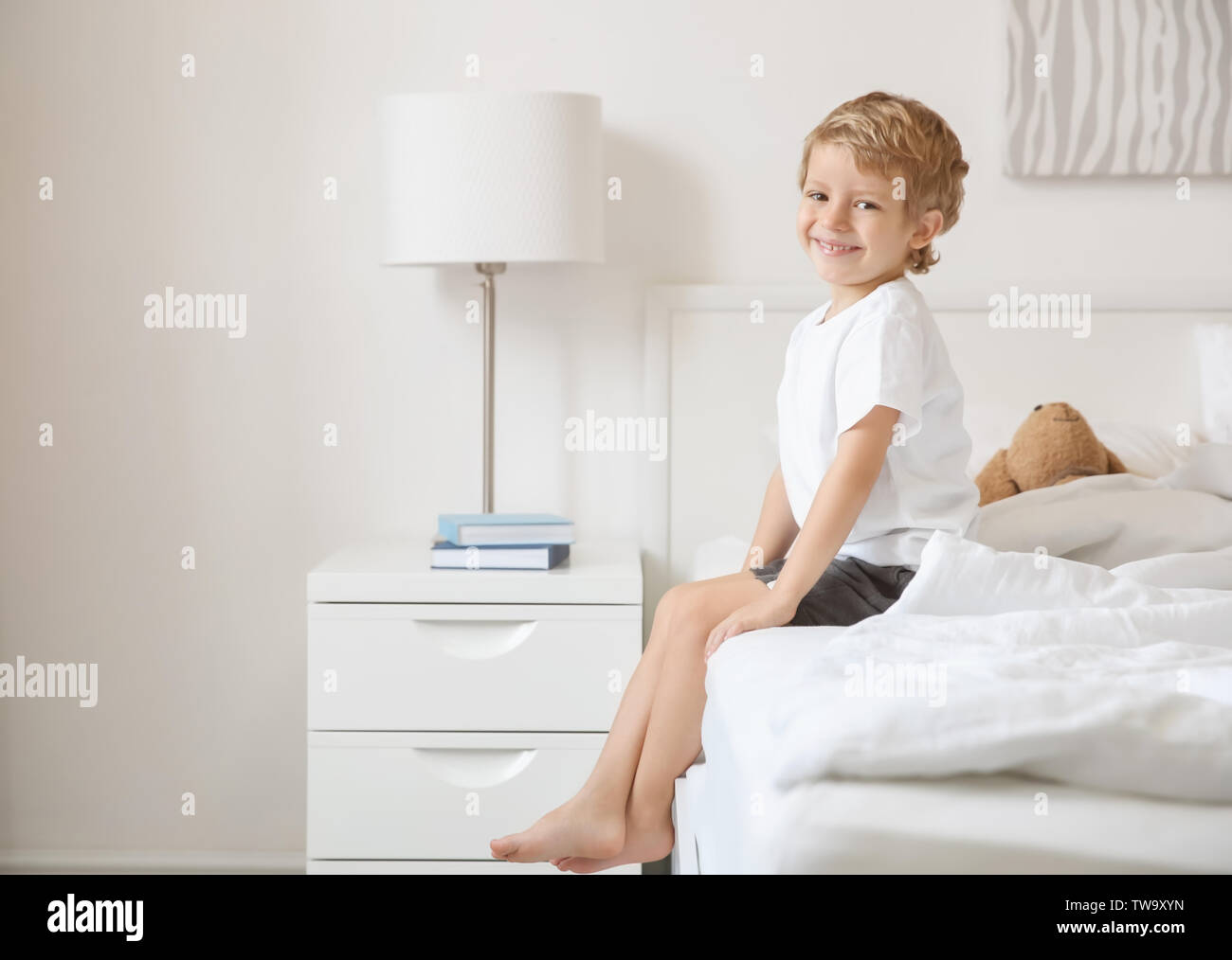 Cute little boy sitting on bed at home Stock Photo - Alamy
