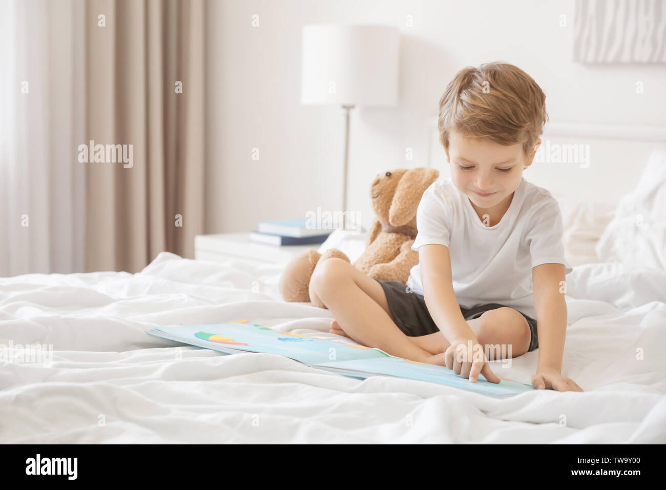Cute boy reading book on bed at home Stock Photo - Alamy