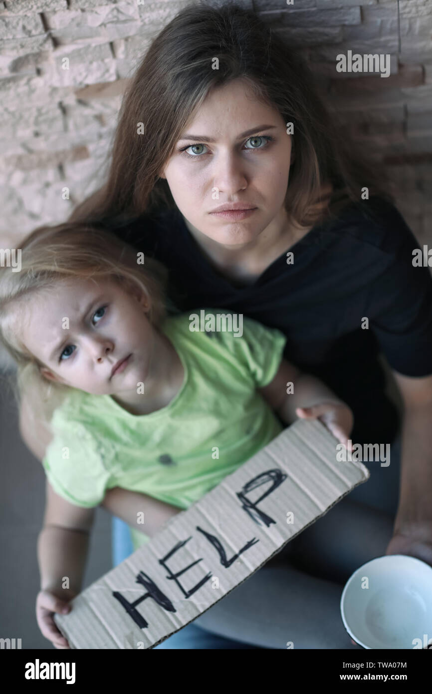 Homeless poor woman and her little daughter sitting near brick wall and ...