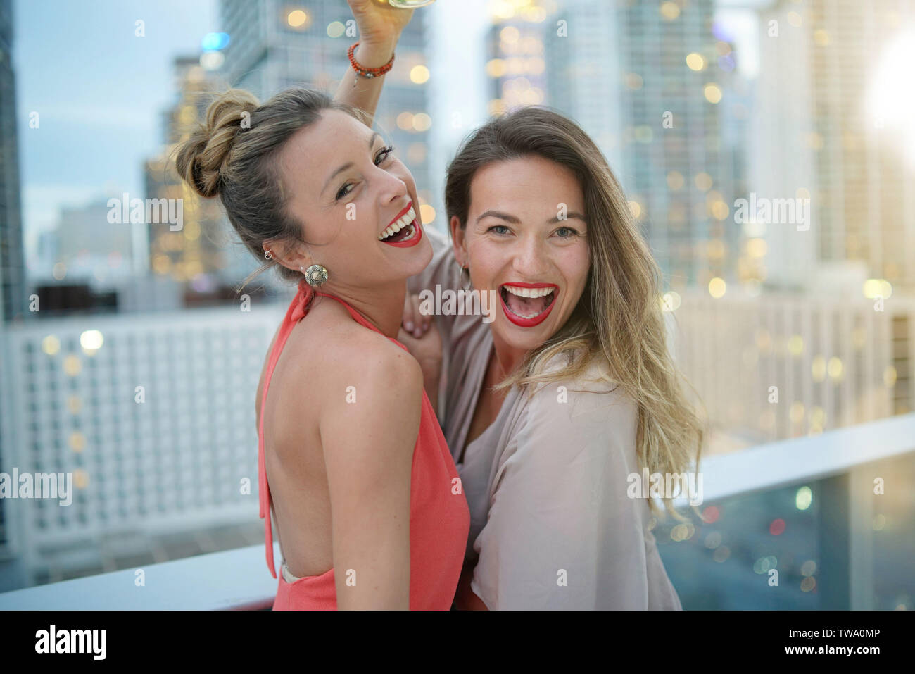 Two gorgeous friends having fun on rooftop bar in city at night fall ...