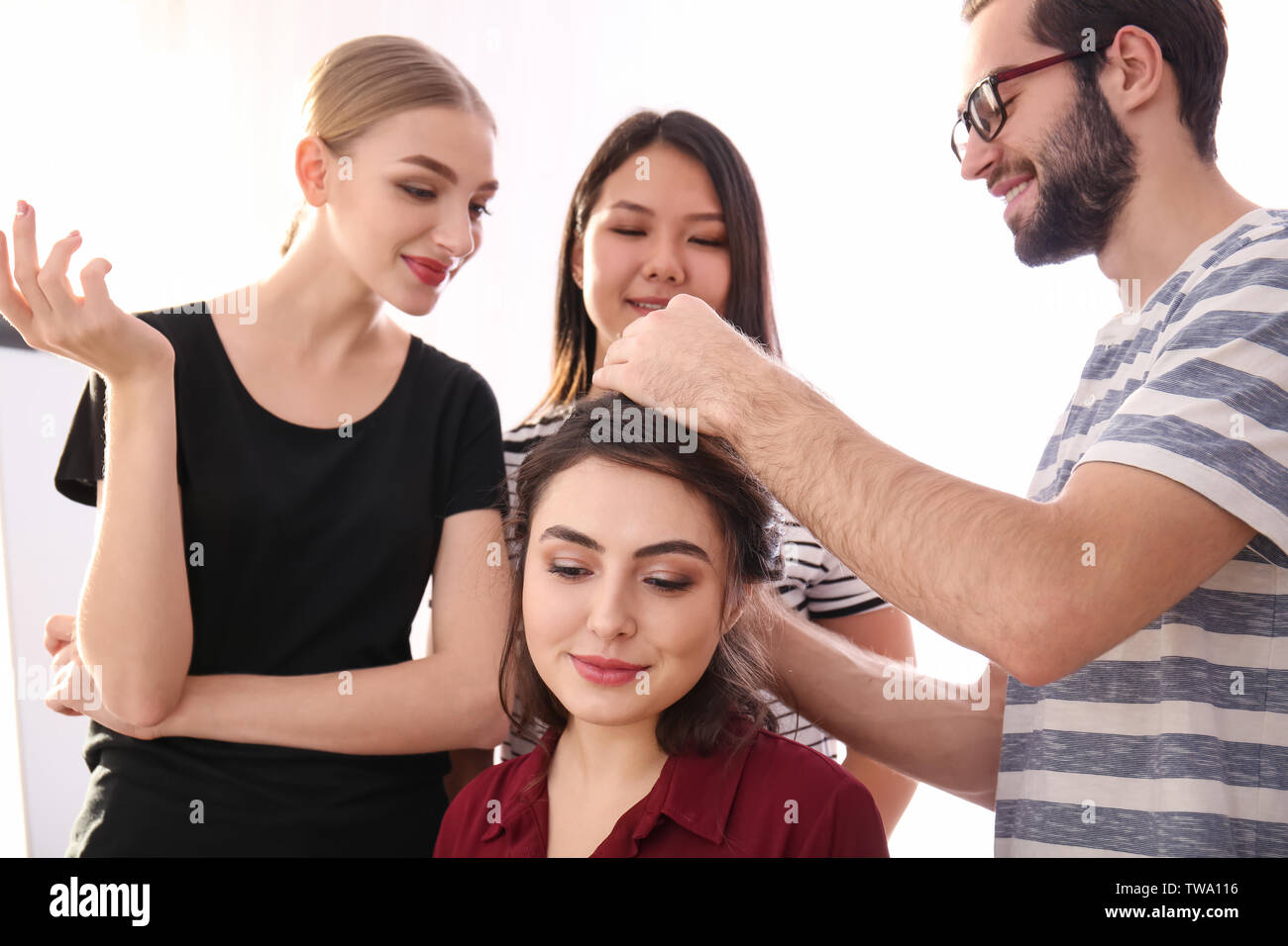 Professional hairdresser and trainees working with client in salon ...