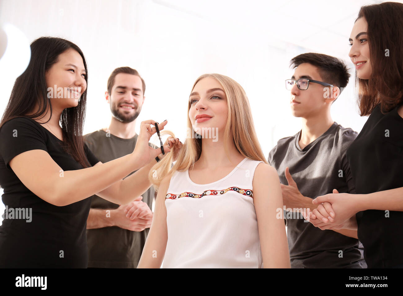 Professional hairdresser and trainees working with client in salon ...