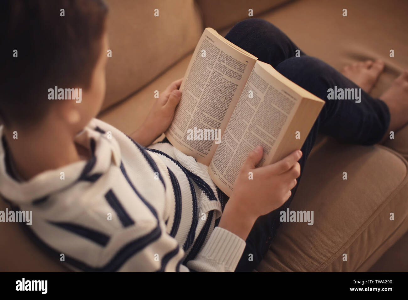 KYIV, UKRAINE - JANUARY 03, 2018: Little boy reading Bible on sofa ...