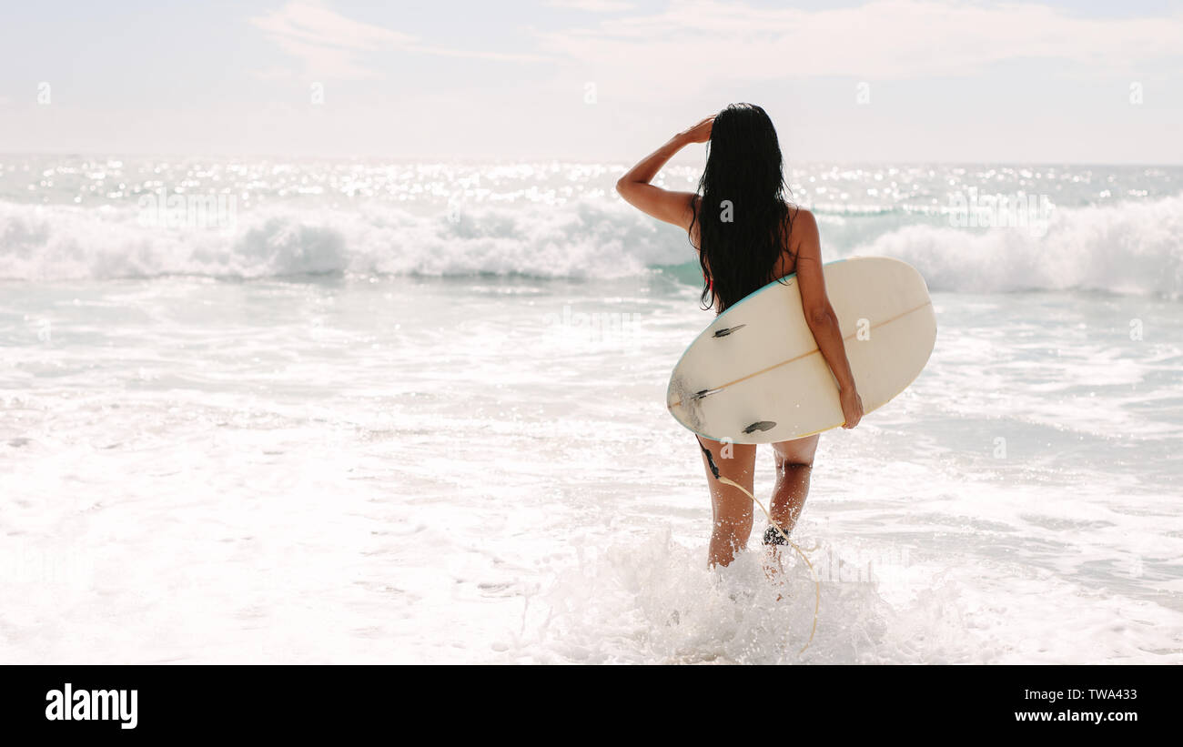 Rear view of woman with surf board walking in to the sea. Caucasian ...