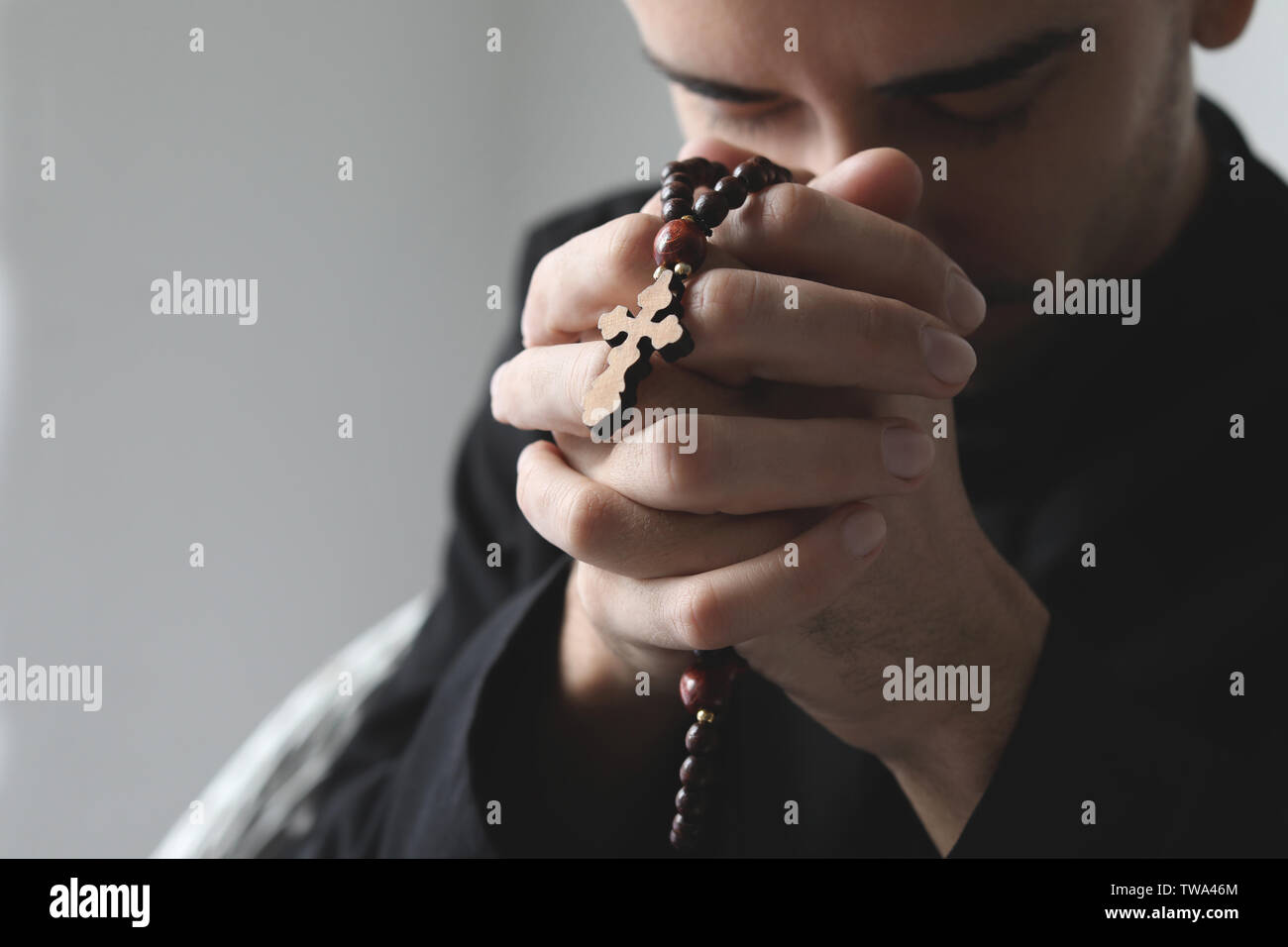 Young praying priest with rosary beads on light background, closeup ...