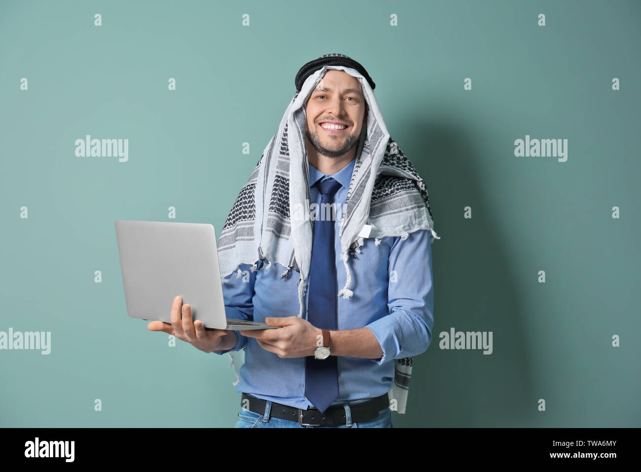 Muslim businessman in traditional clothes with laptop on color ...