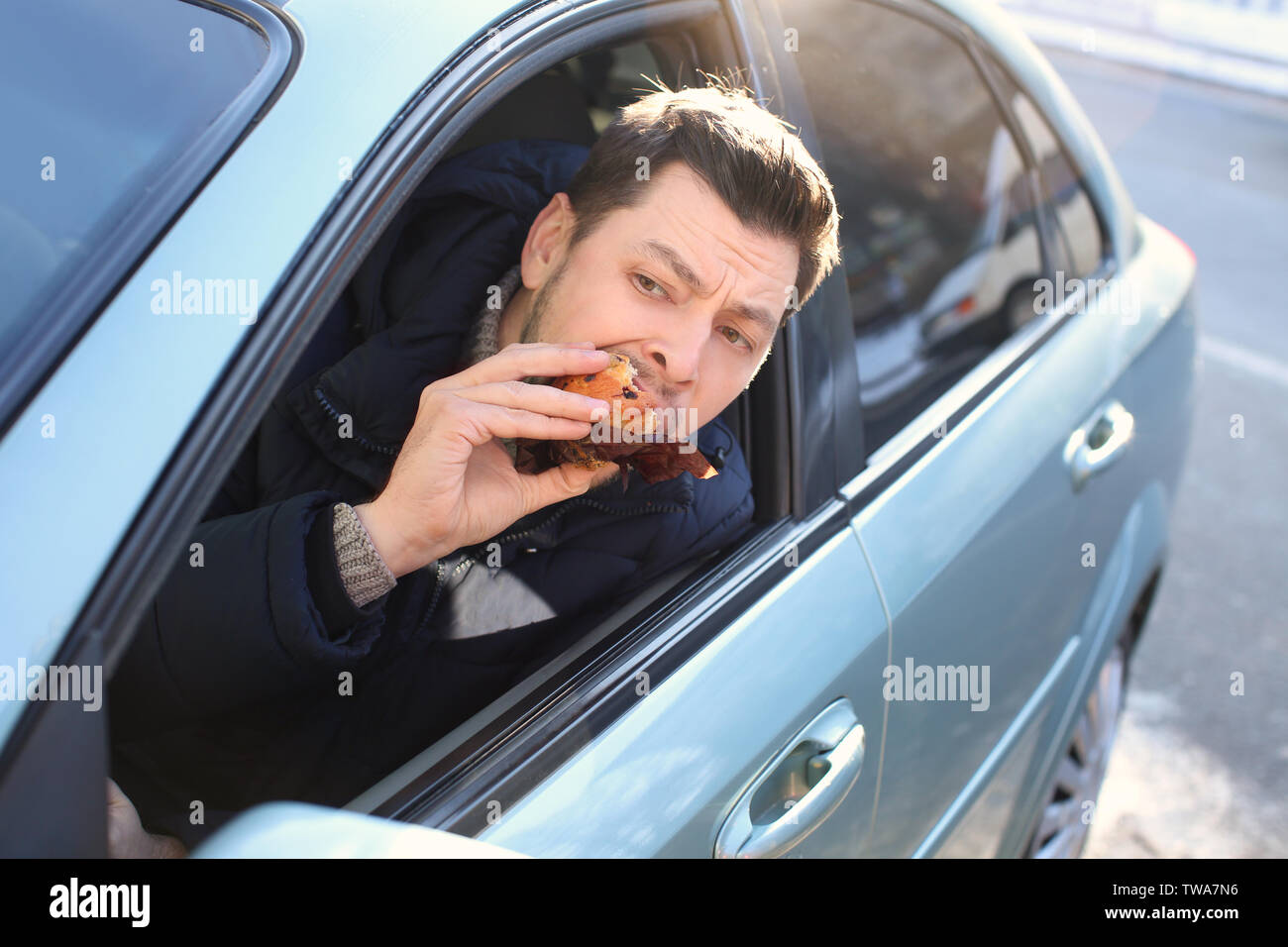 Young man eating muffin inside car in traffic jam Stock Photo - Alamy