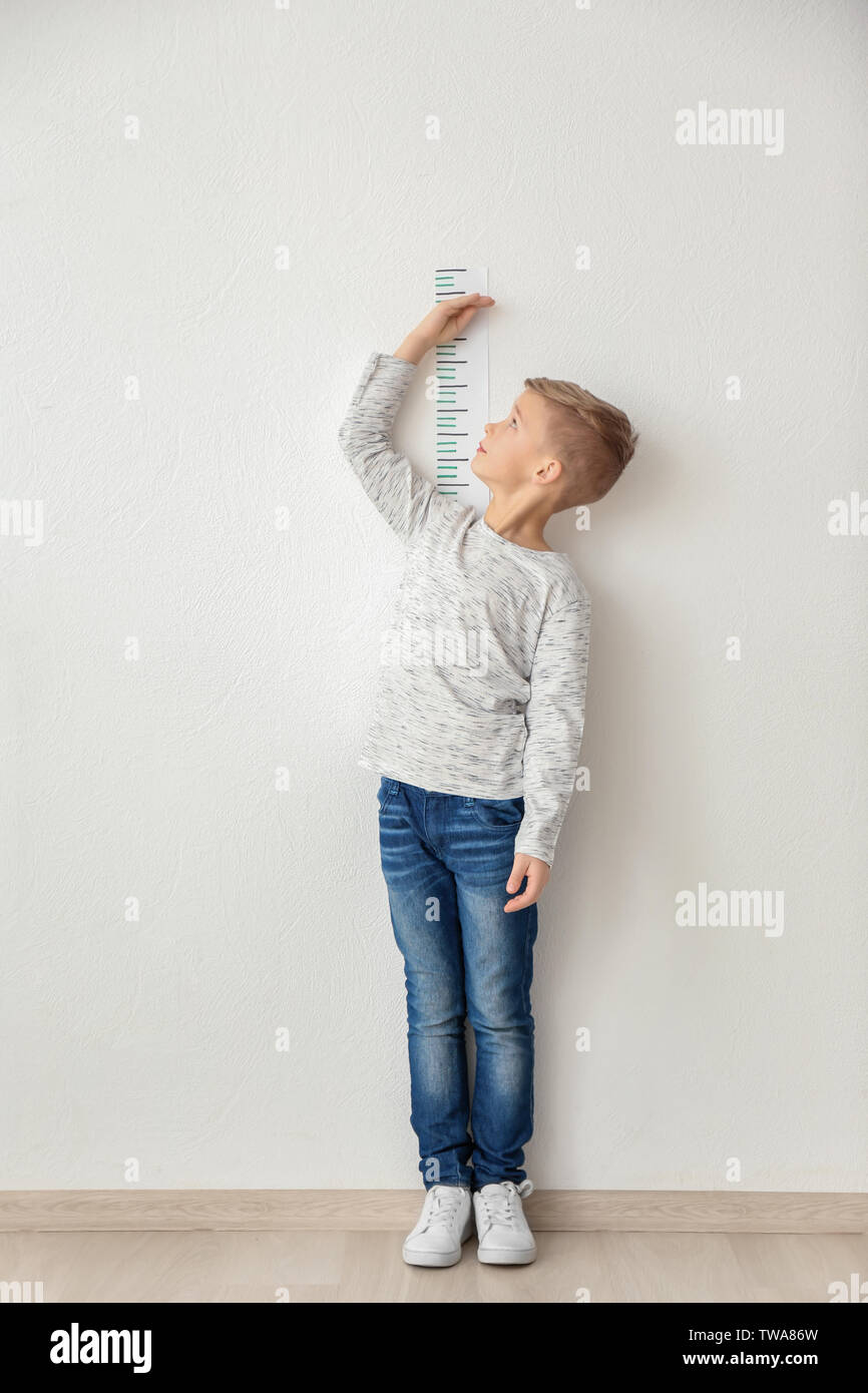 Cute little boy measuring height near light wall Stock Photo - Alamy