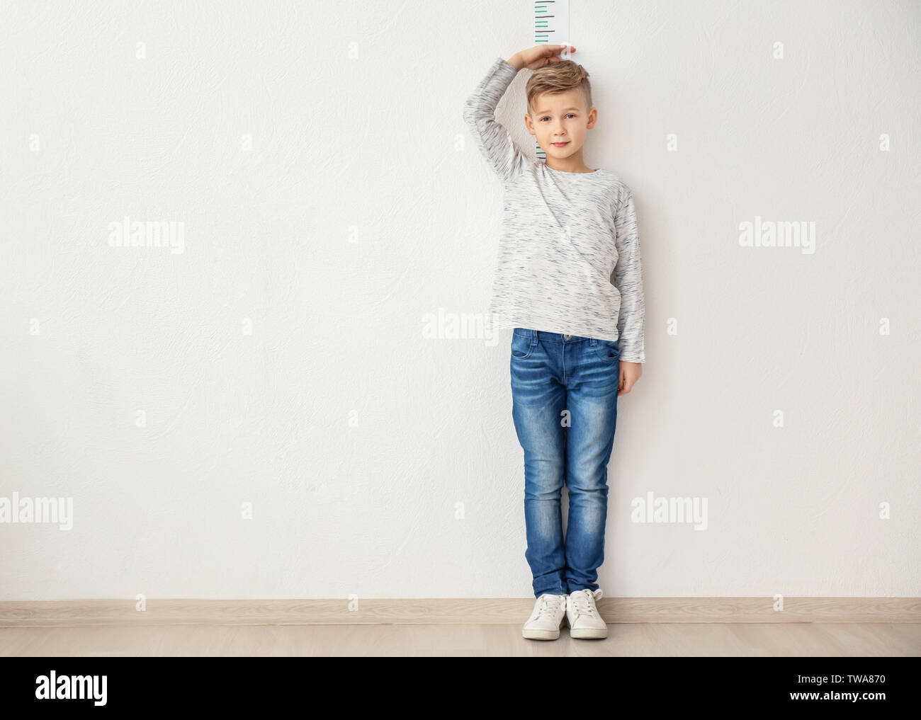 Cute little boy measuring height near light wall Stock Photo - Alamy