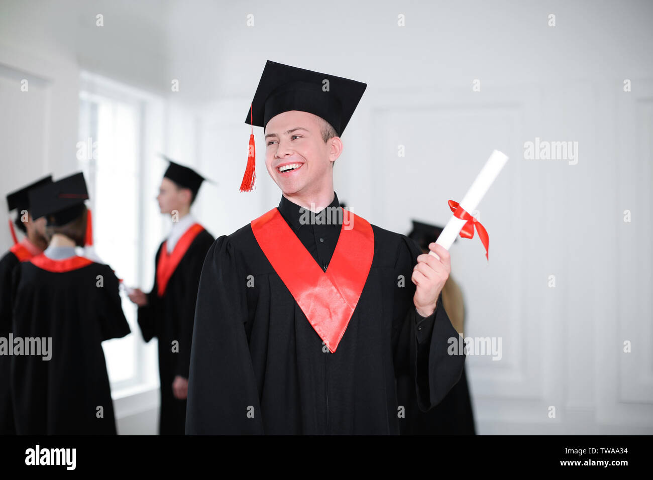 Happy student in bachelor robe with diploma indoors. Graduation day ...