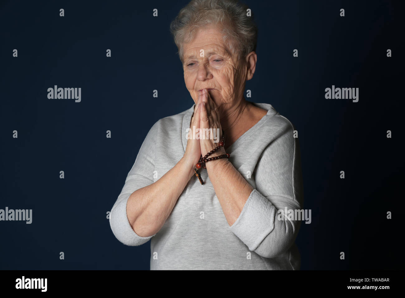 Religious elderly woman praying on dark background Stock Photo - Alamy