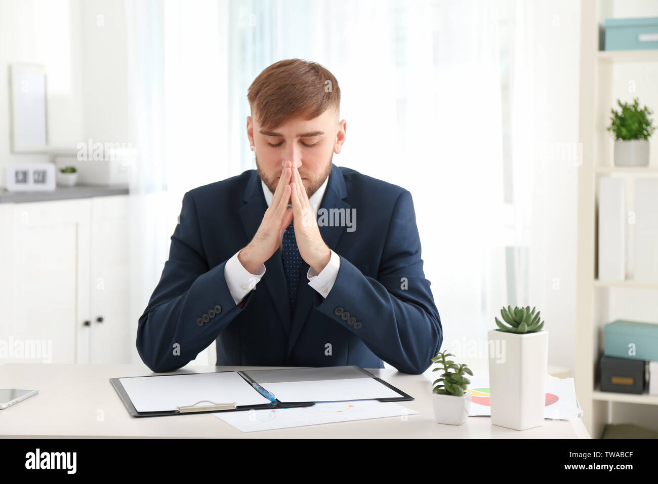 Religious young businessman praying at table in office Stock Photo - Alamy