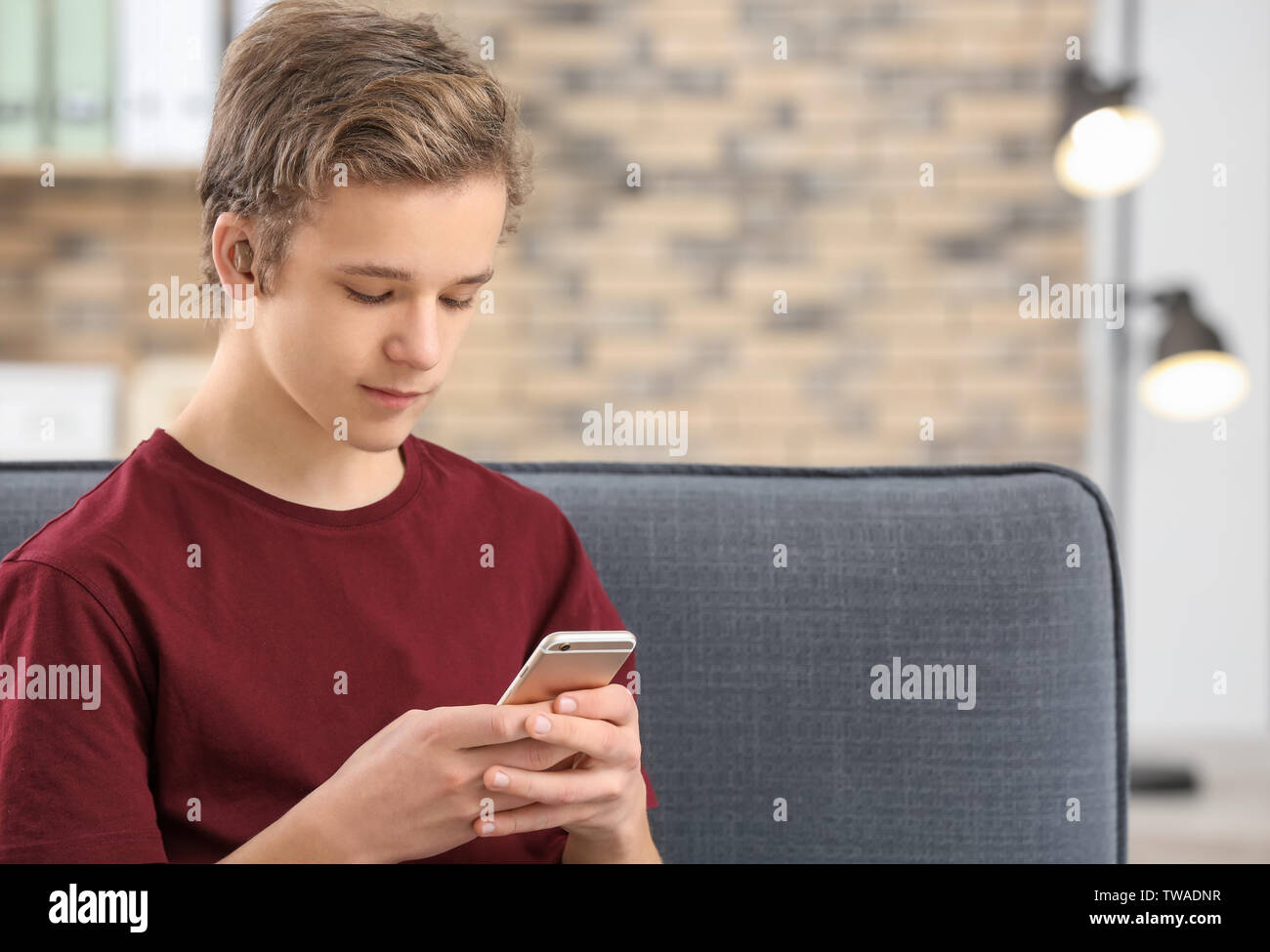 Teenage boy with hearing aid using smartphone indoors Stock Photo - Alamy