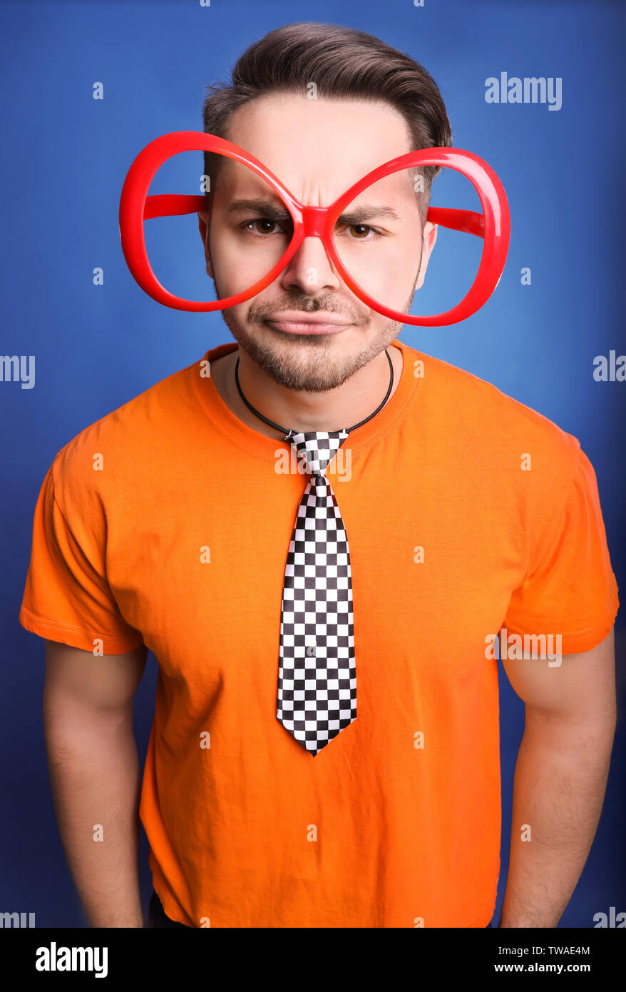 Young man in funny glasses on color background. April fool's day ...