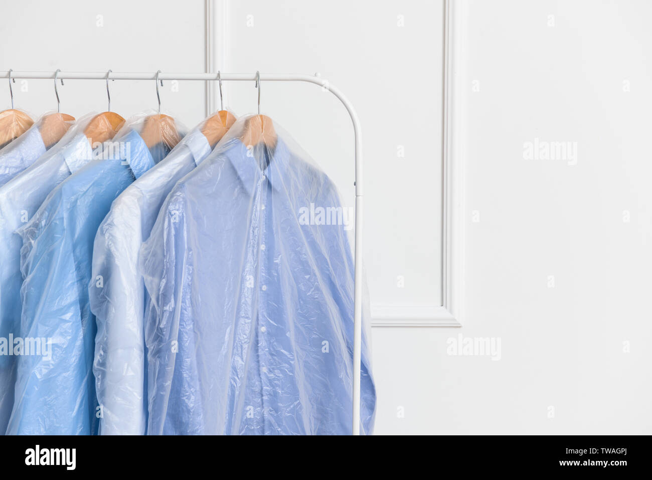 Rack with clothes after dry-cleaning near white wall Stock Photo - Alamy