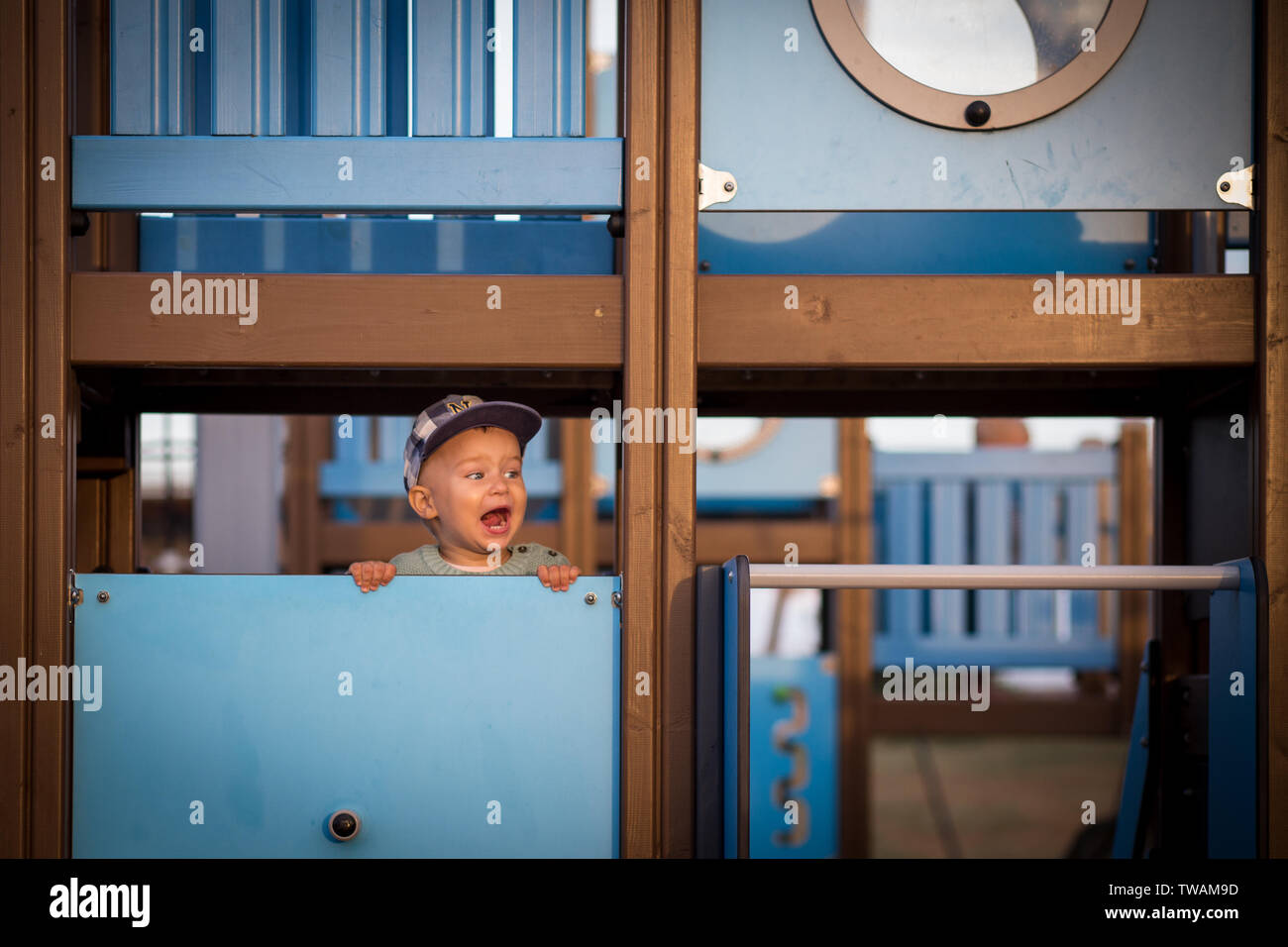 Little boy, wearing cap, shouting at somebody, standing behind wall, on ...