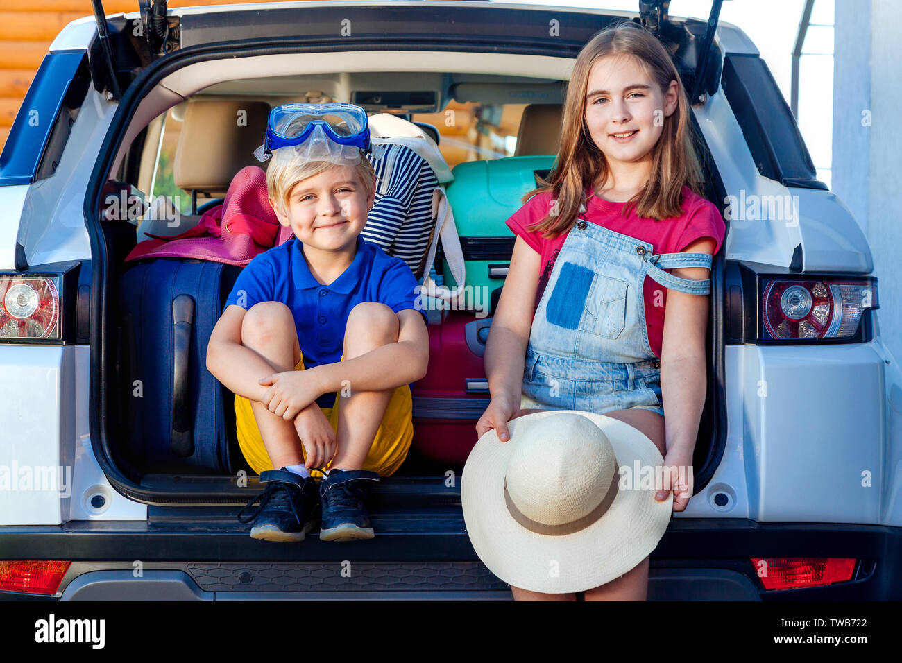 Little sister and brother are sitting in the trunk of a car with ...