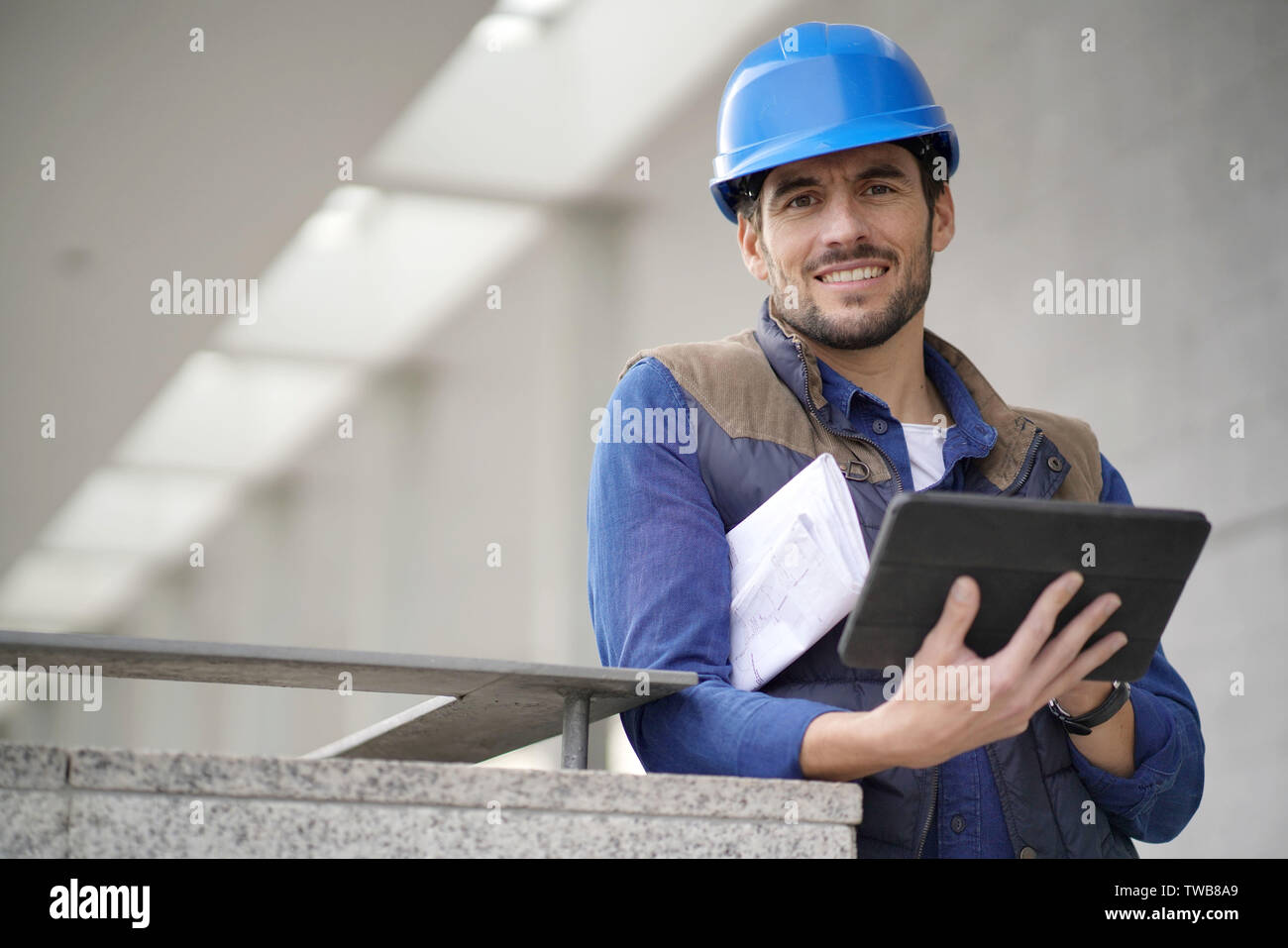 Attractive builder outdoors with tablet and blueprints smiling at ...