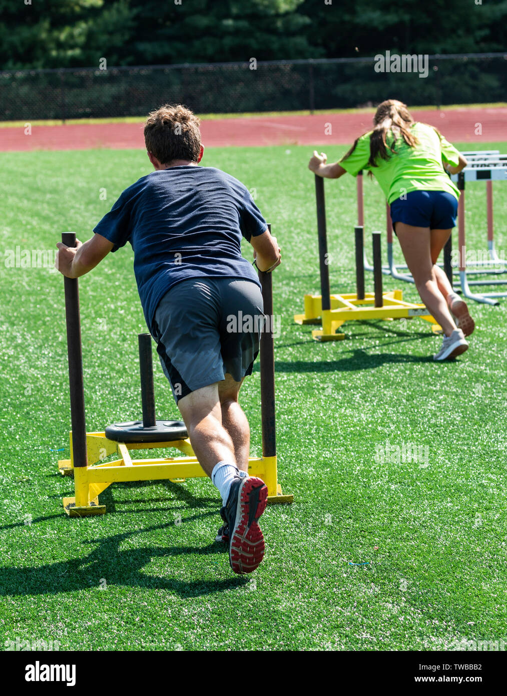 Two athletes pushing heavy yellow sleds across a green turf field ...