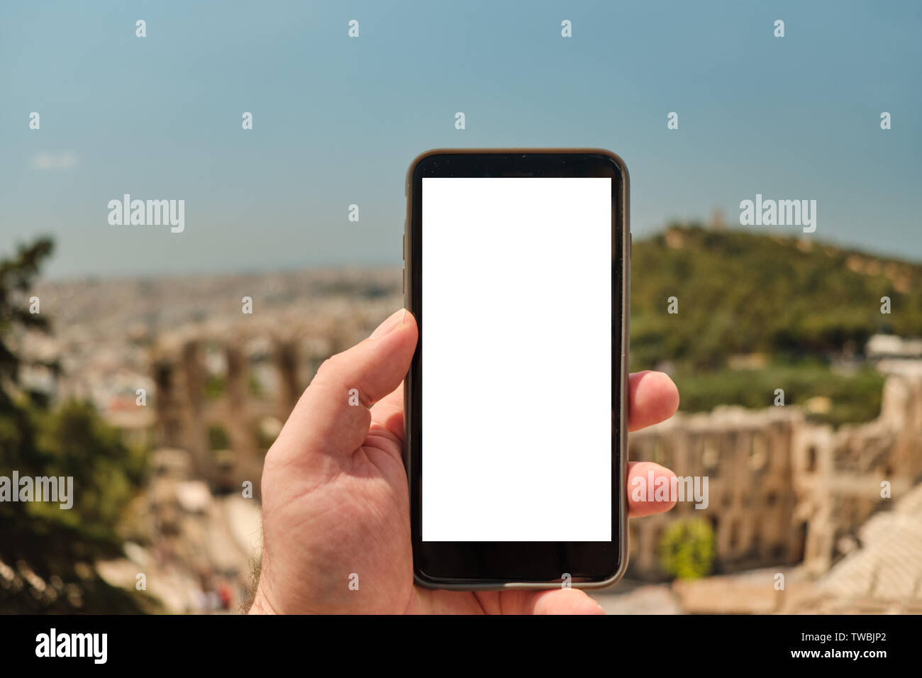 hand of man holding smart phone in front of the ancient area o the ...