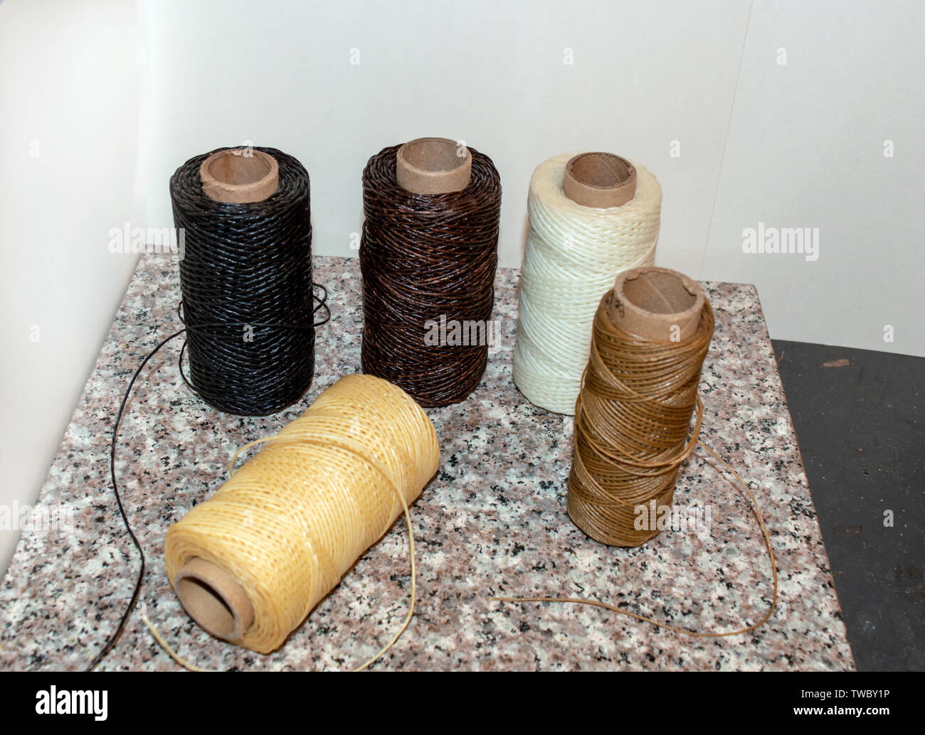 A variety of colors of leather crafting threads sit on a smooth quartz ...