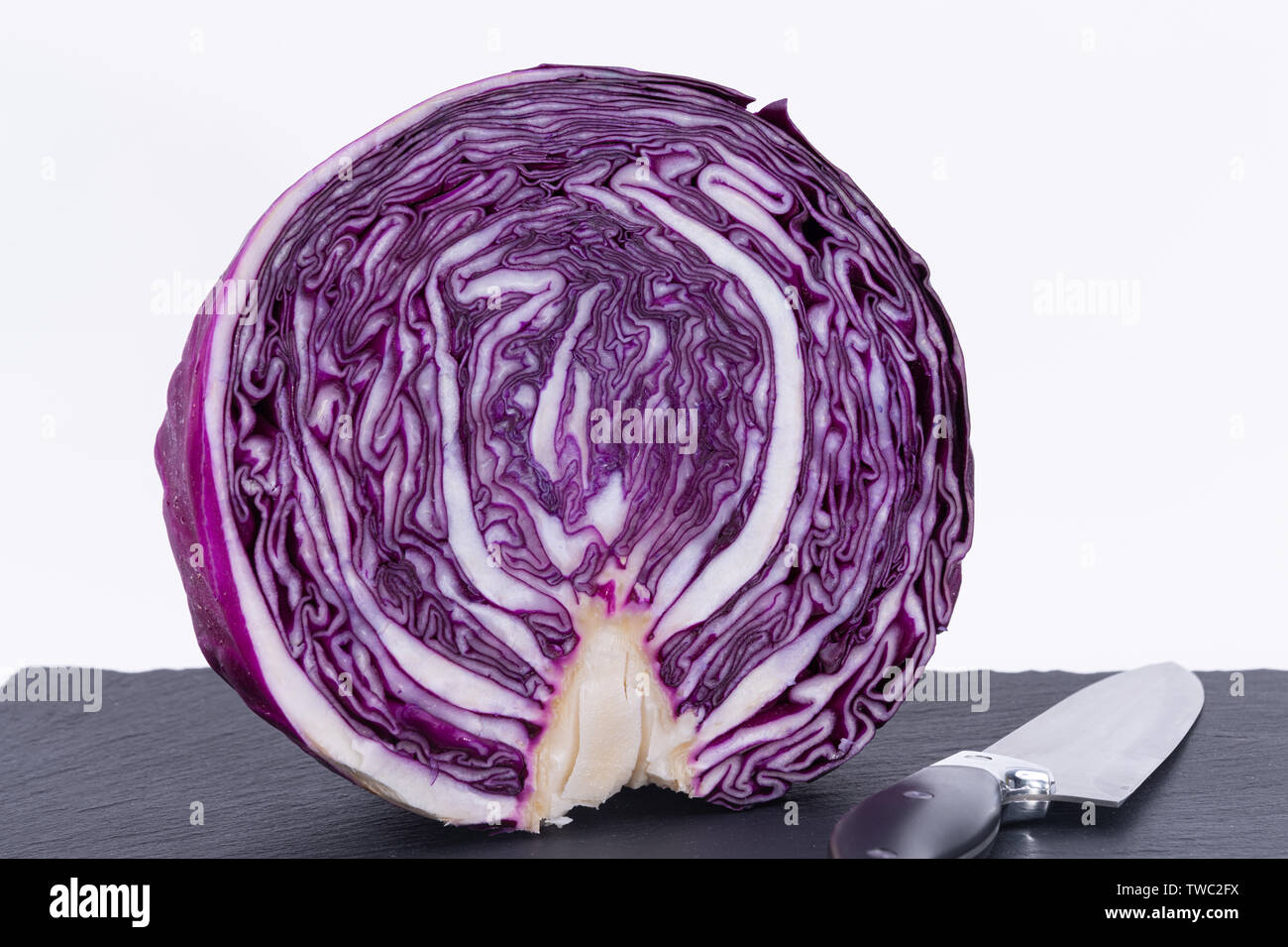 A purple cabbage cut in half accompanied by a knife on a black cutting ...