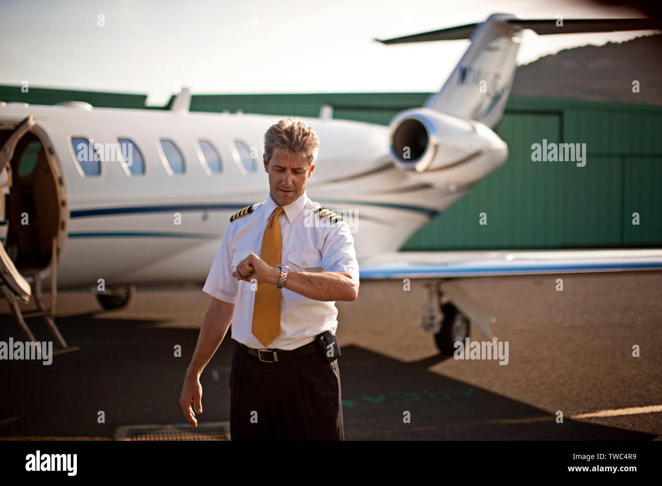 A pilot looking at his watch while standing in front of a private jet ...