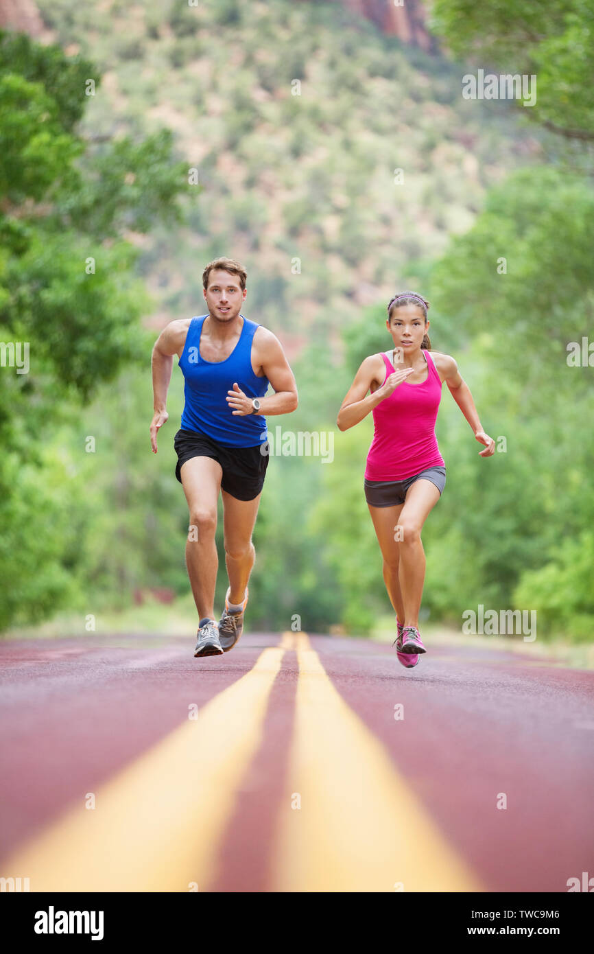Running young mixed race couple sprinting concentrated on road outside ...