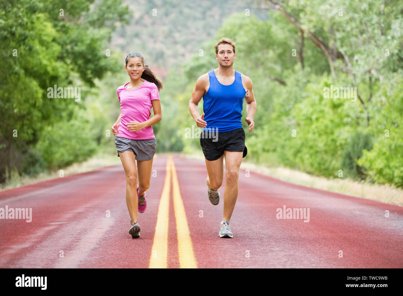 Running young multicultural couple exercising fitness outside on road ...