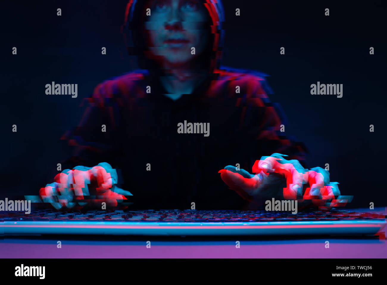 Hacker in the hood working with computer typing text in dark room. Image with glitch effect ...