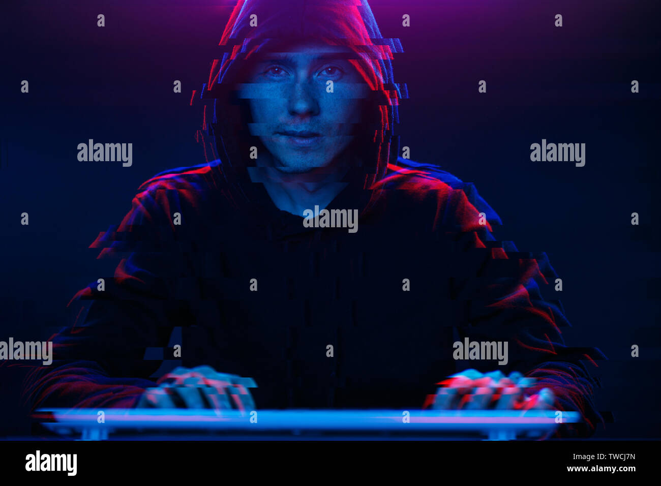 Hacker in the hood working with computer typing text in dark room. Image with glitch effect ...