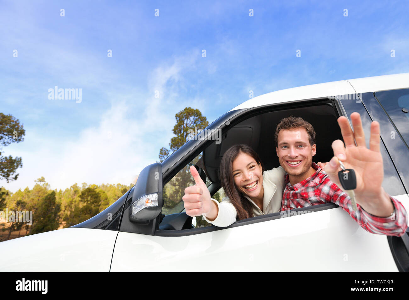 New car - happy couple showing car keys driving having fun on road trip ...