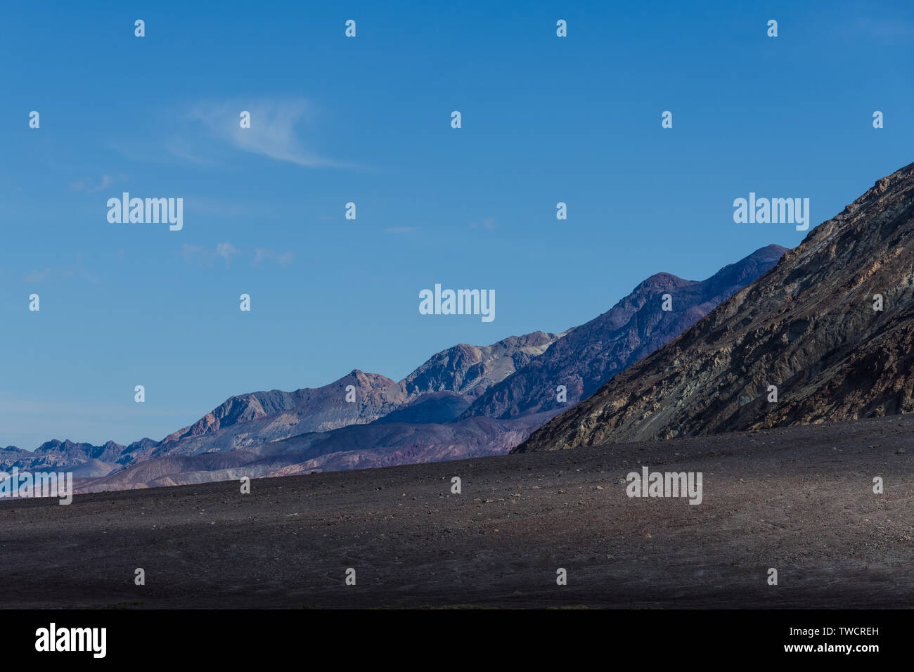 Barren desert landscape with dark volcanic earth and a mountain range ...