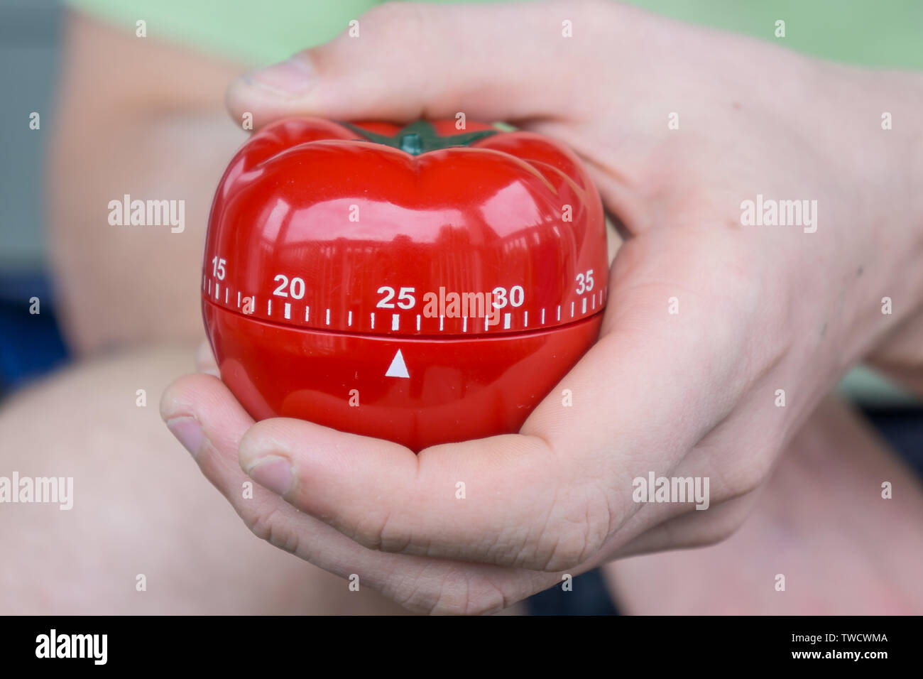 Mechanical red tomato kitchen timer set to 25 minutes, gripped by one ...