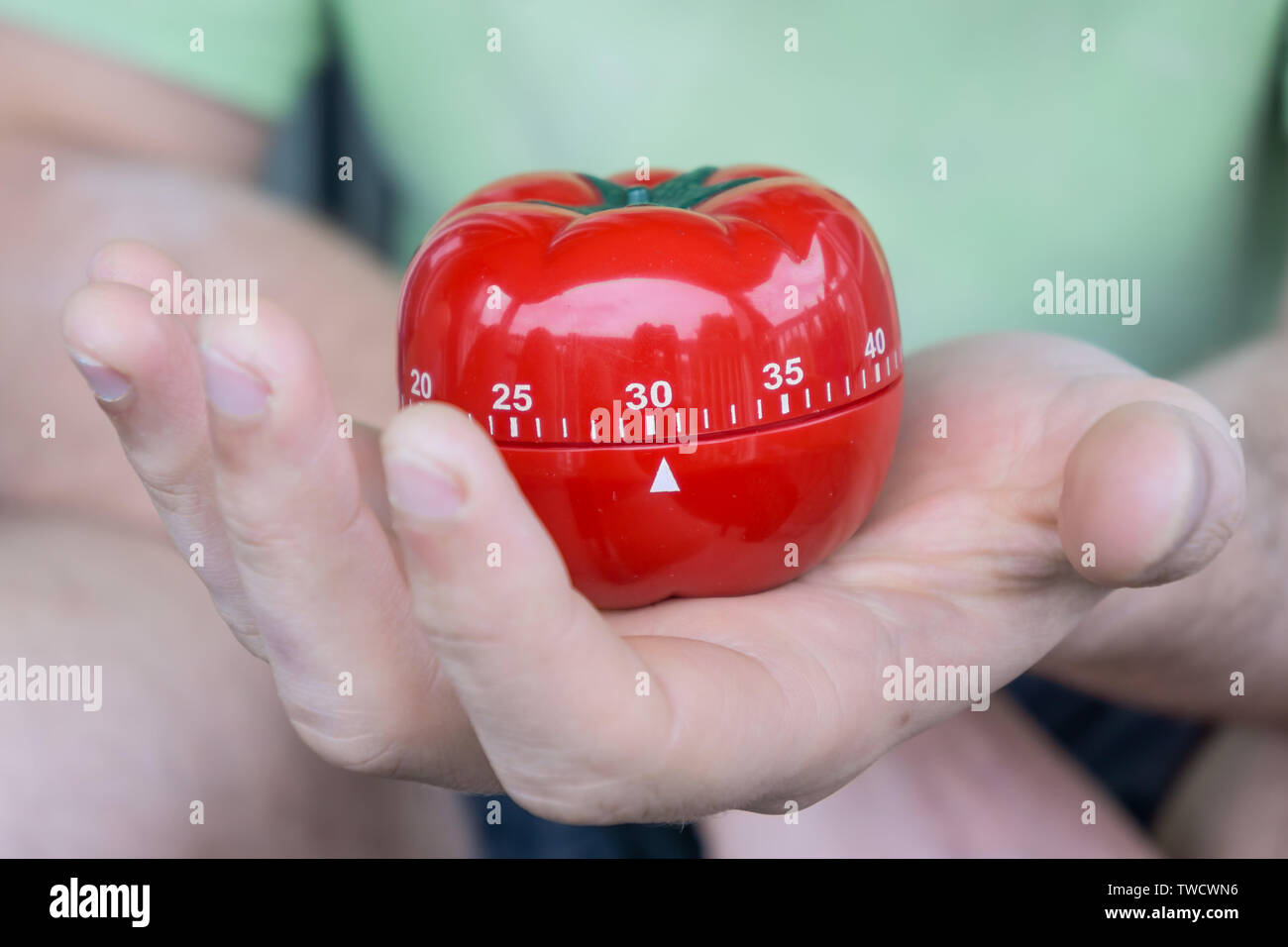 Mechanical red tomato kitchen timer set to 30 minutes, held by a person ...