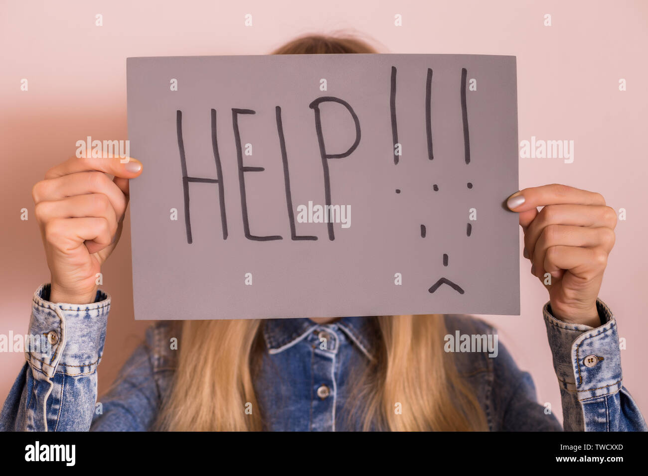 Woman holding paper with word help and sad face while standing in front ...