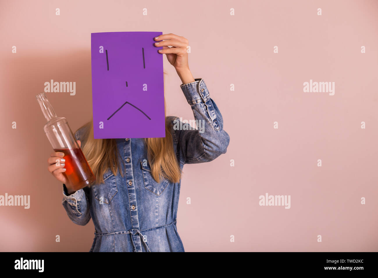 Woman holding alcohol and sad face on paper in front of the wall ...