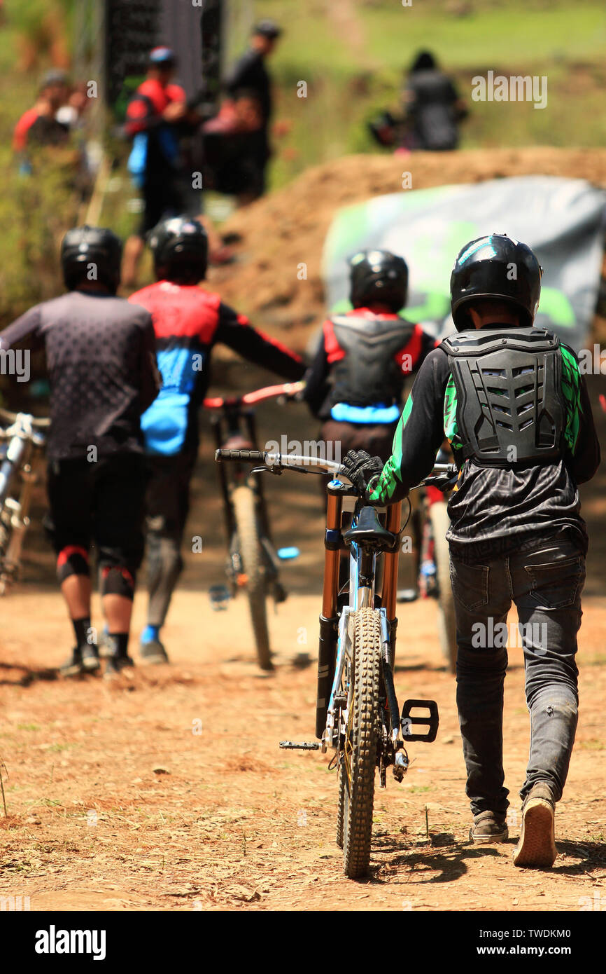 A group of downhill cyclist walking to the finish line with their bikes ...