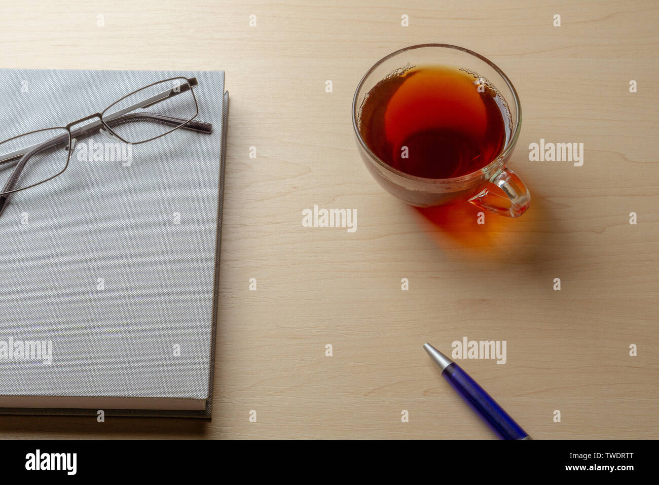 Gray diary, cup of tea, blue pen and glasses on a brown table ...