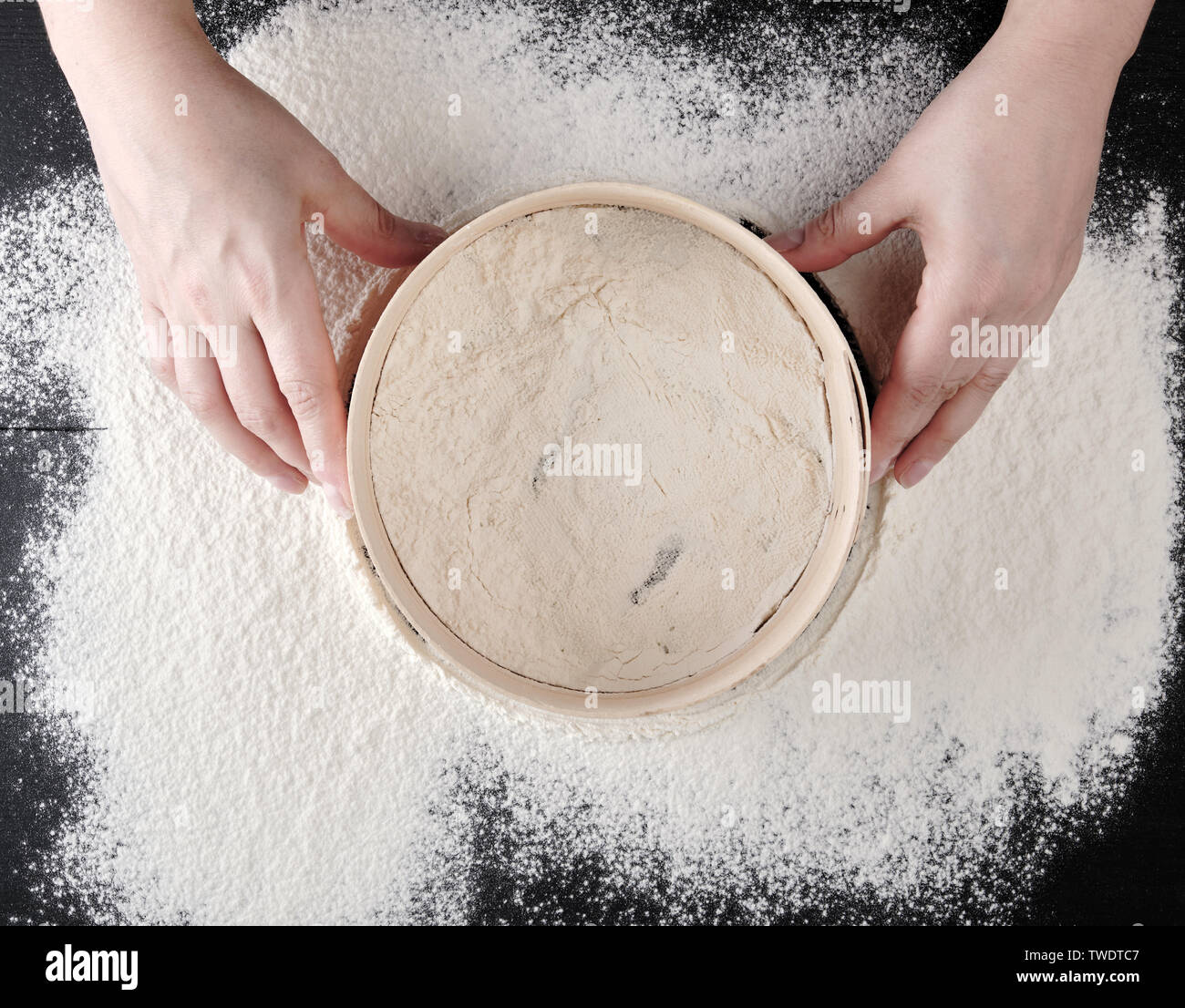 women's hands hold a round wooden sieve and sift white wheat flour, top ...