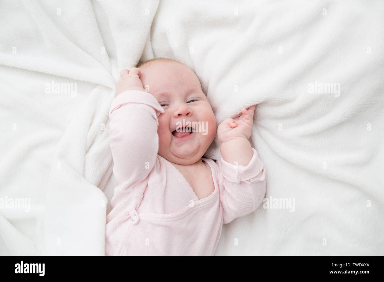 Newborn baby girl posed on her back, on blanket of fur, smiling looking ...