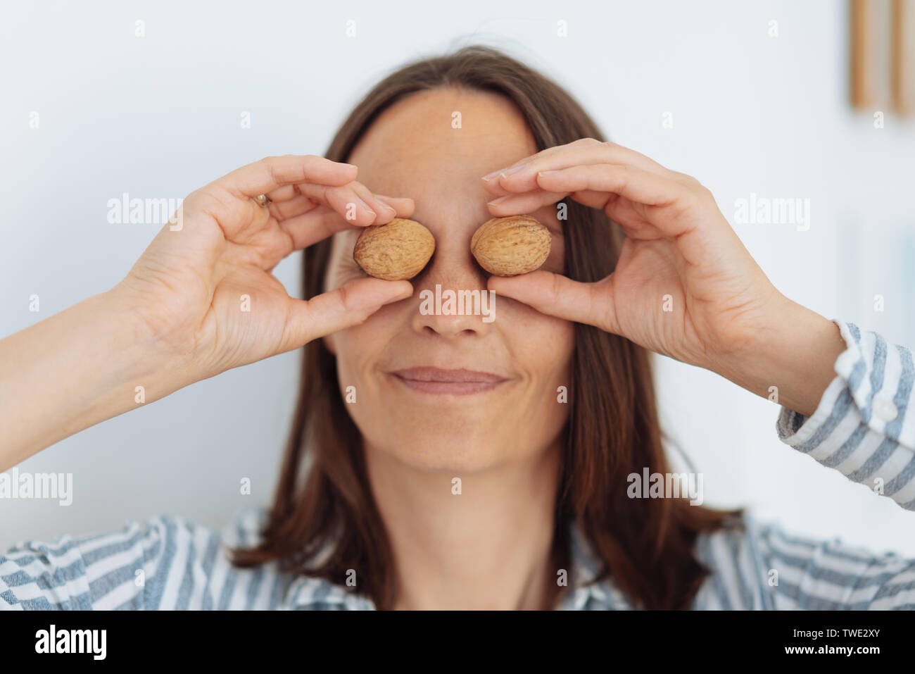 Playful woman holding whole fresh walnuts in their shells to her eyes ...