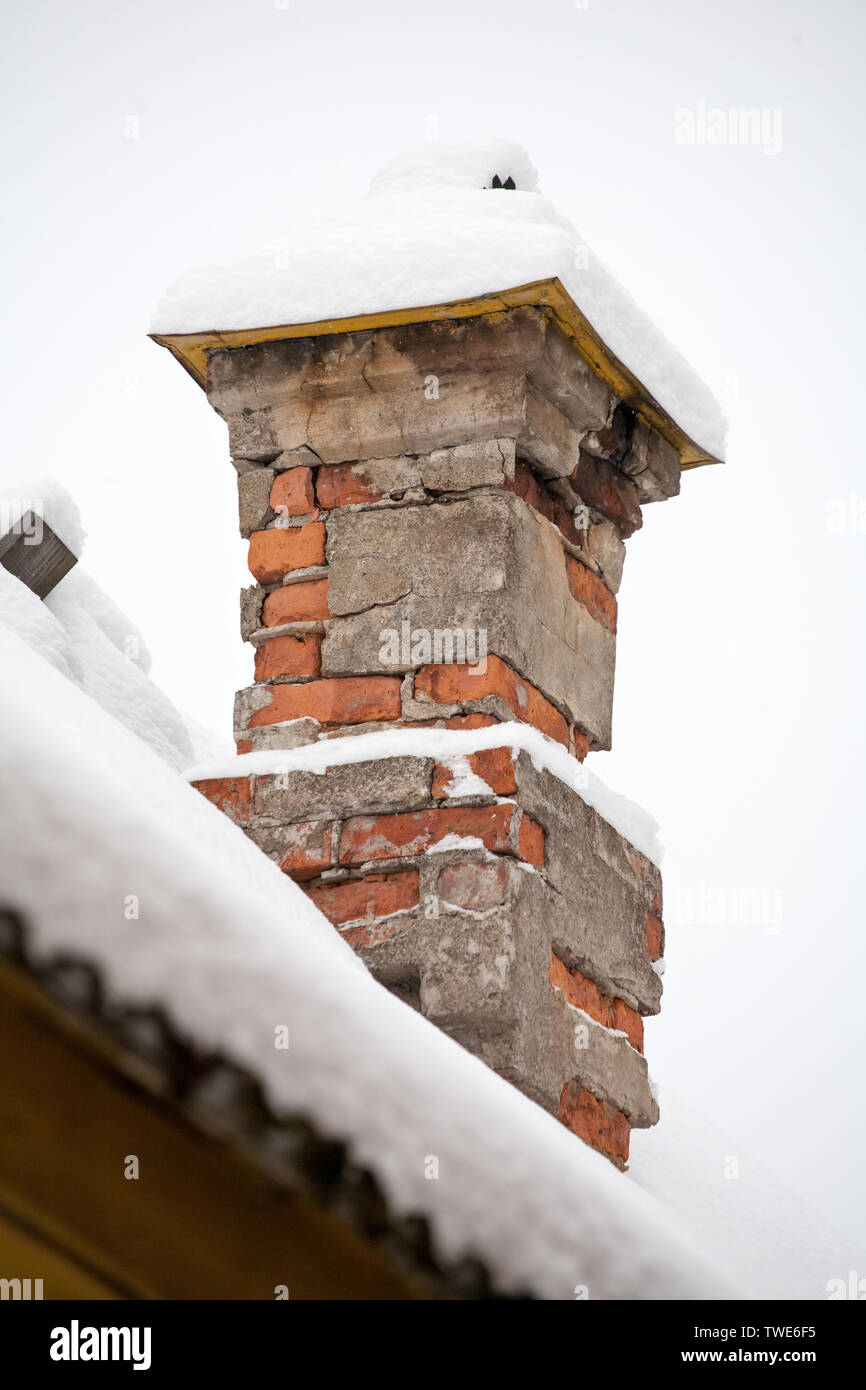 old chapped brick chimney with snow on top on white sky background ...