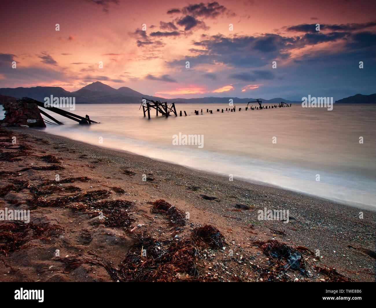 Sand beach with algae and ruined pier into the sea, sunset time, Milos ...